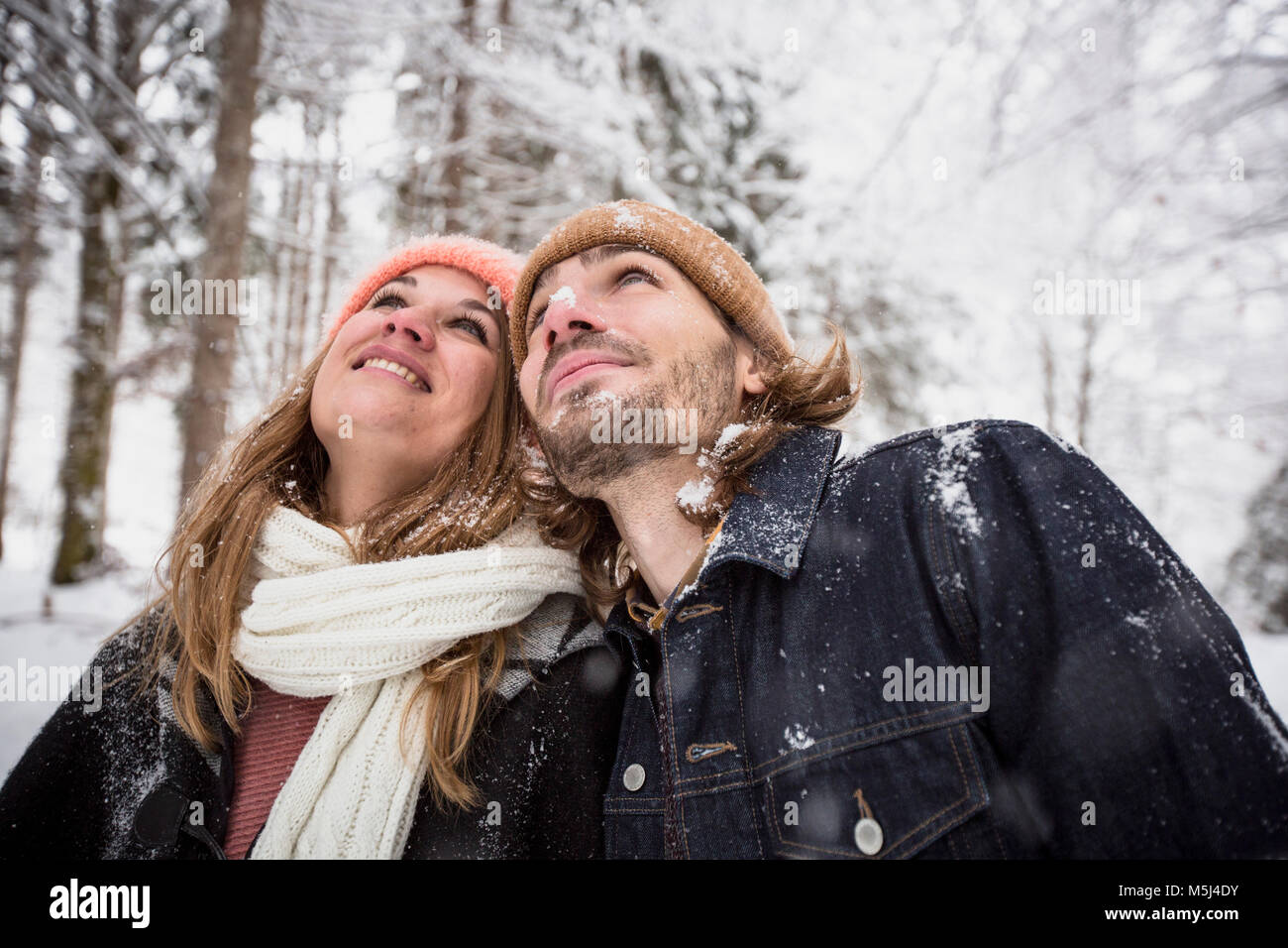 Smiling couple in winter forest watching snow fall Stock Photo - Alamy