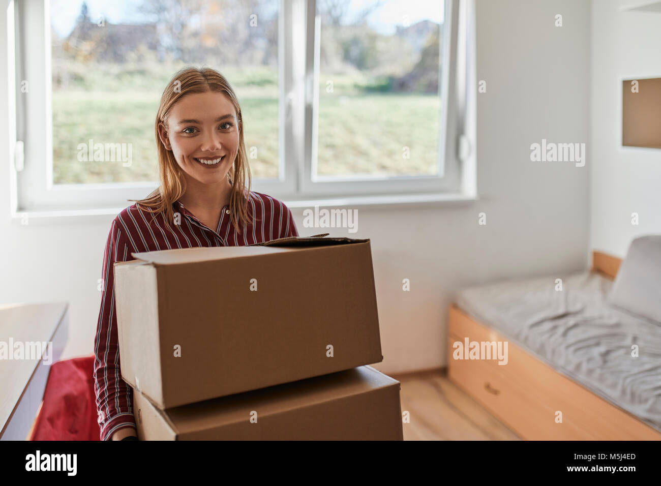 Portrait of smiling young woman carrying cardboard boxes Stock Photo ...