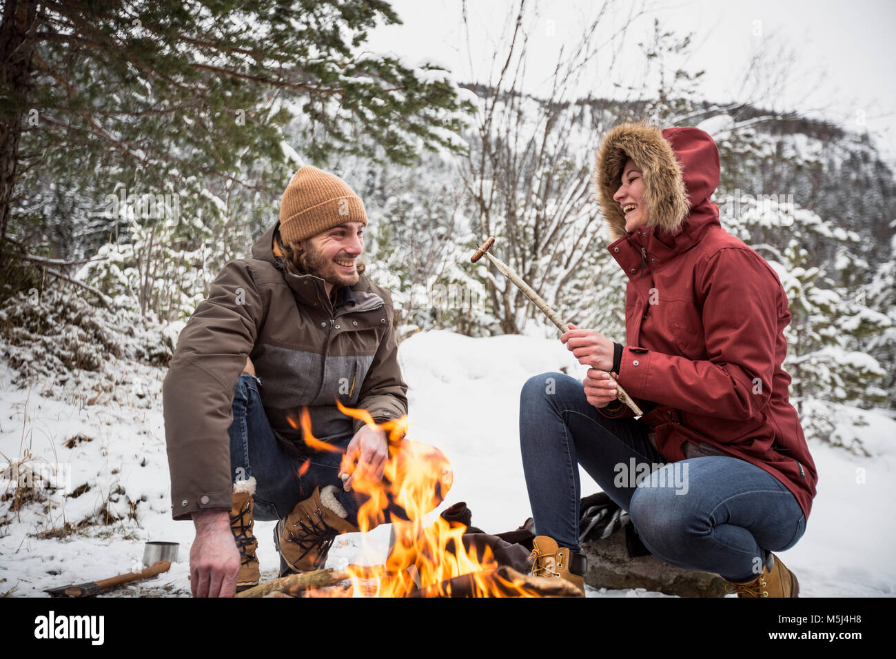Happy couple on a trip in winter having a break at camp fire Stock ...