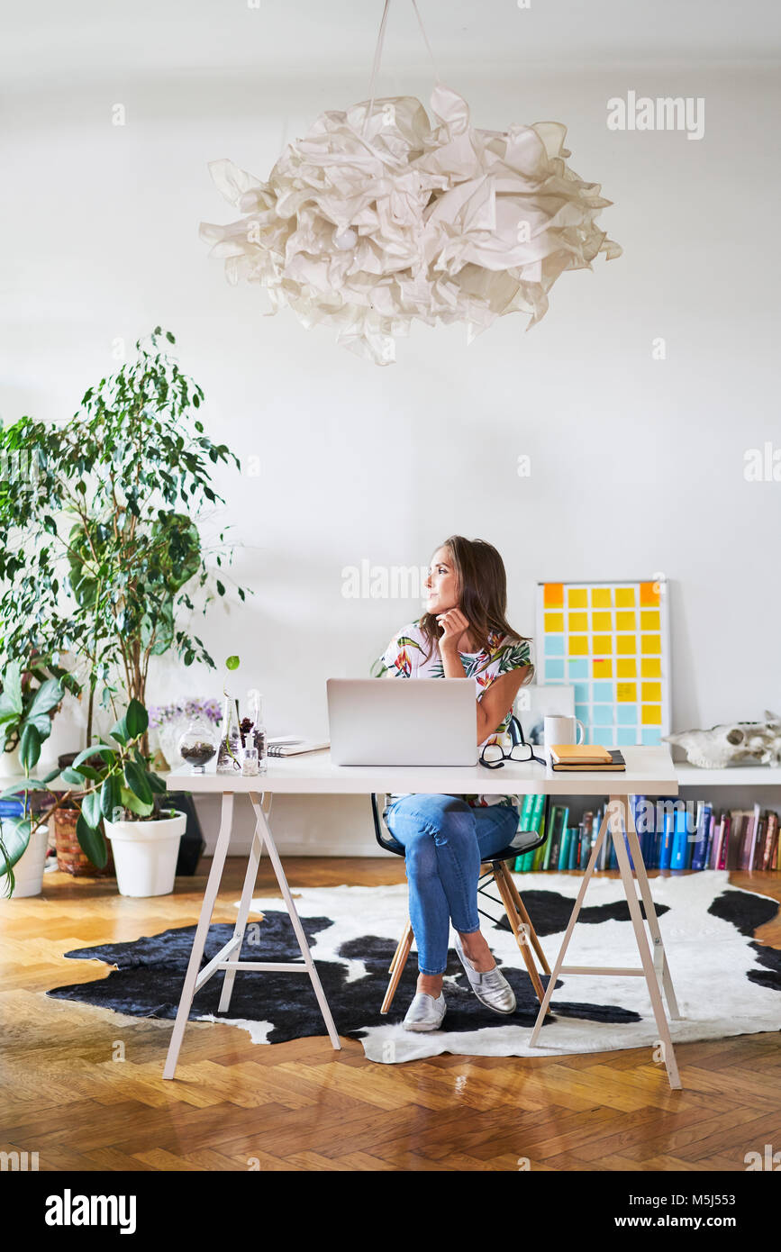 Young woman at home with laptop on desk looking sideways Stock Photo ...