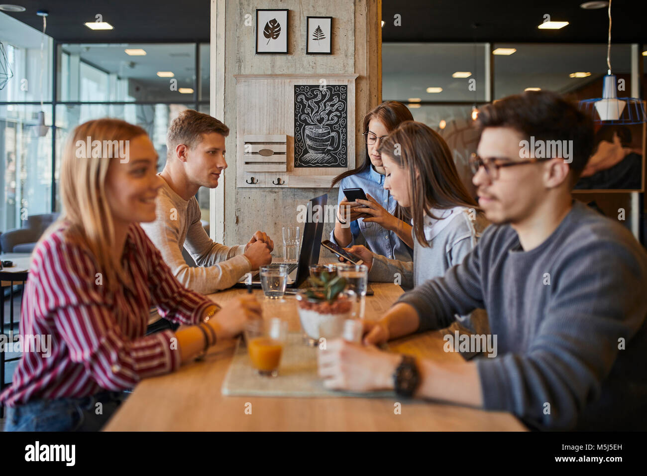 Group of friends sitting together in a cafe with laptop, smartphones ...