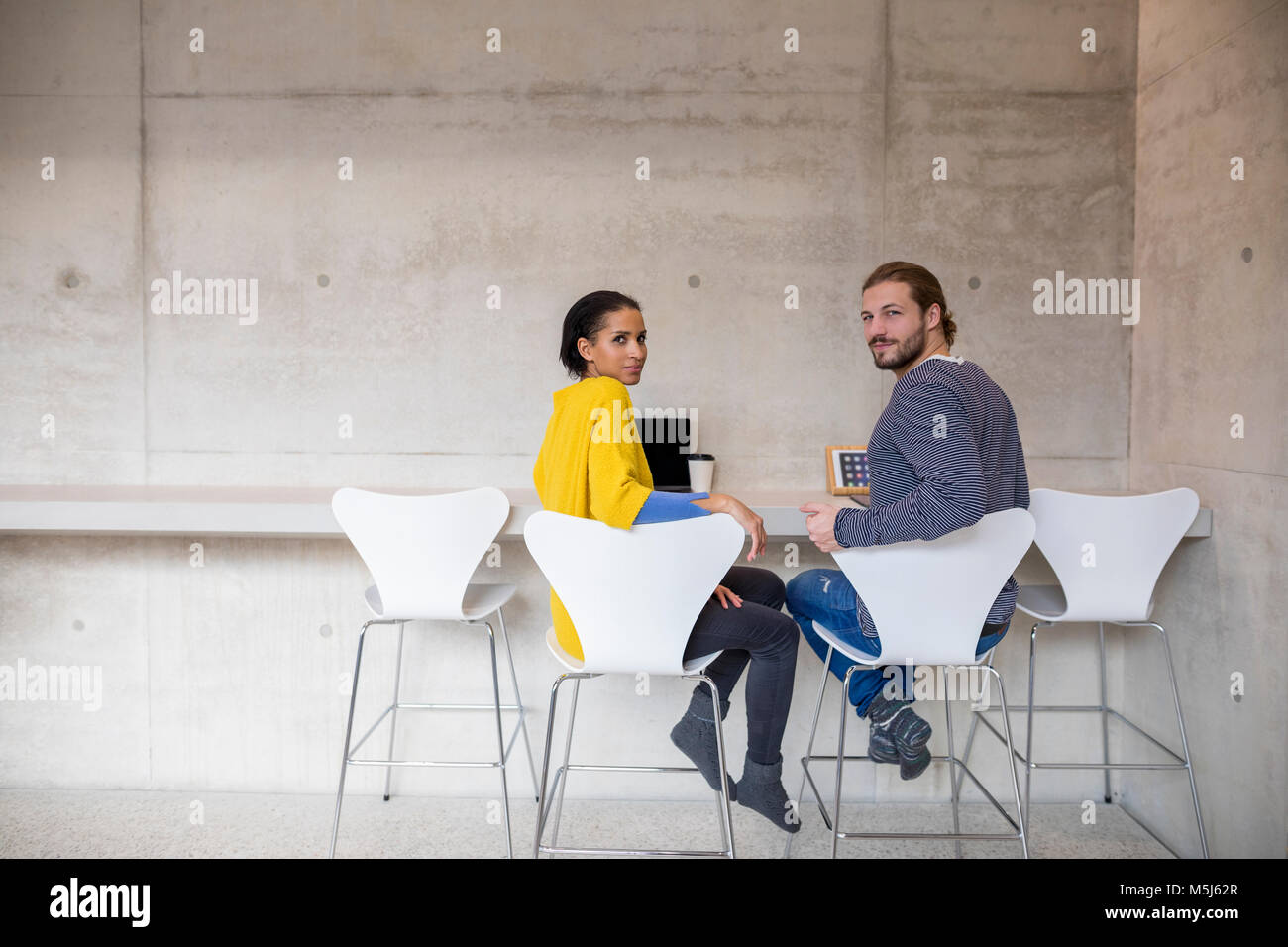 Young man and woman using moblie devices in concrete room Stock Photo ...