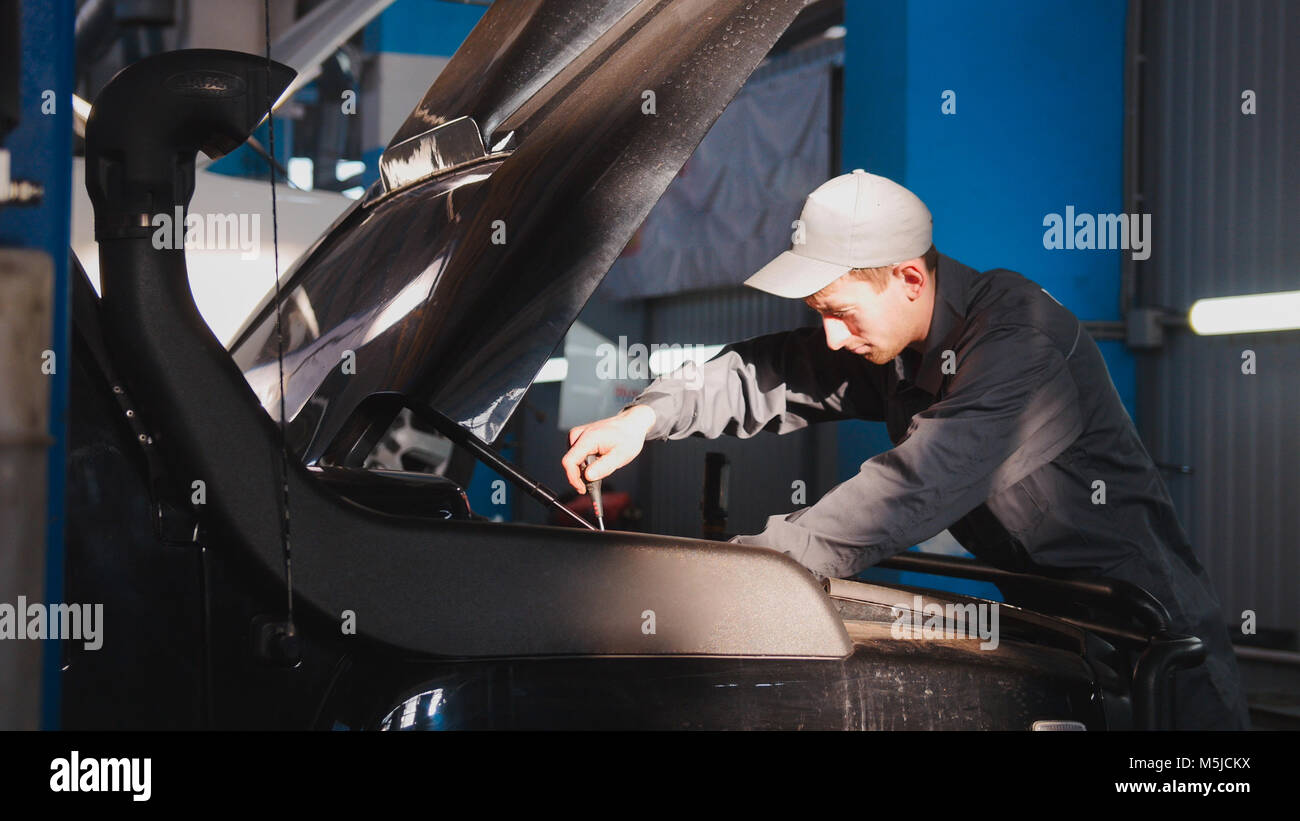 Mechanic male unscrews with a screwdriver in hood of the car for SUV ...