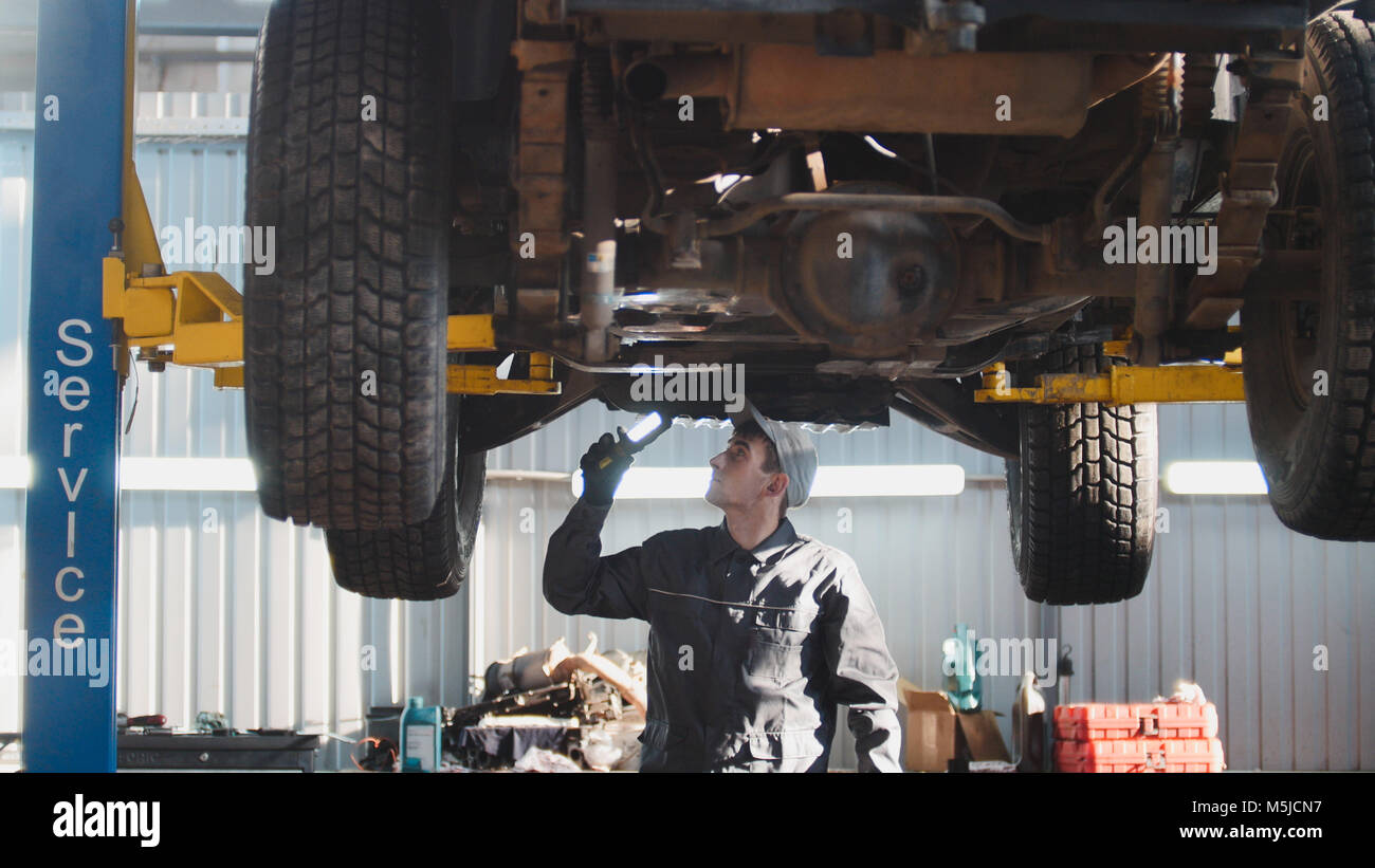 Mechanic with thr lamp is checking the bottom of SUV car in garage ...