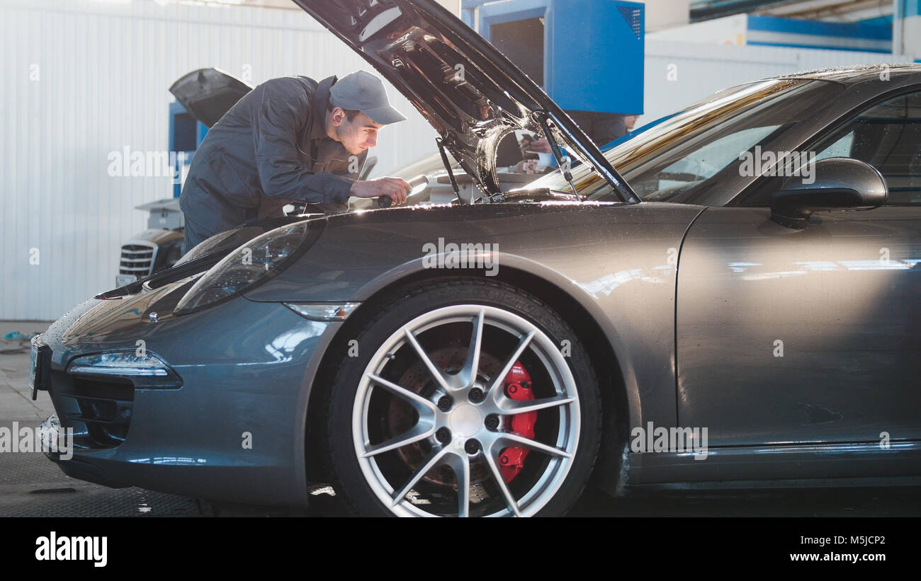 Mechanic male in automobile garage checking hood of the luxury sportcar ...