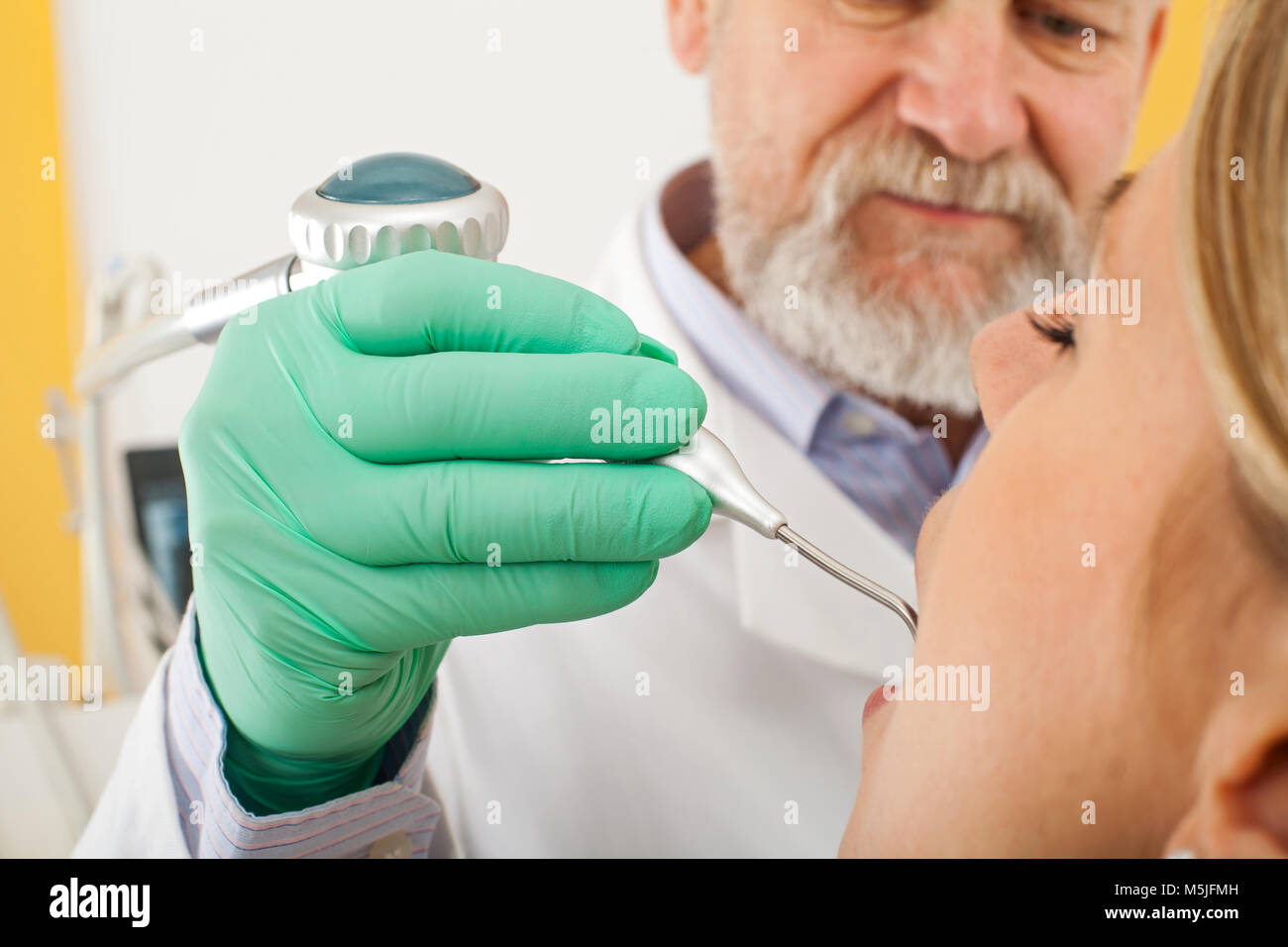 Mature dentist cleaning young smoking patient's denture with air flow ...