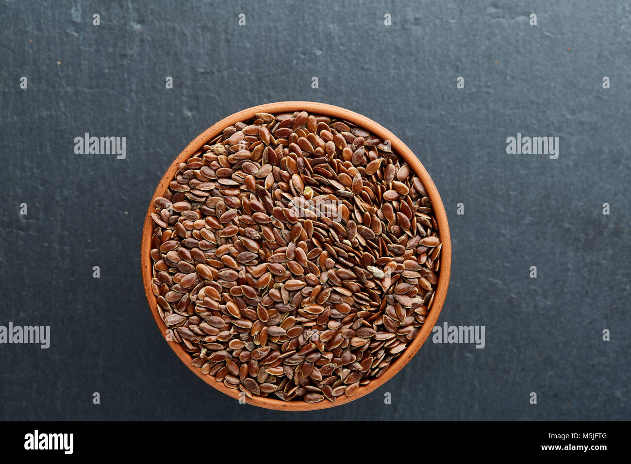 Narural raw flax seeds in a ceramic clay bowl isolated on dark ...