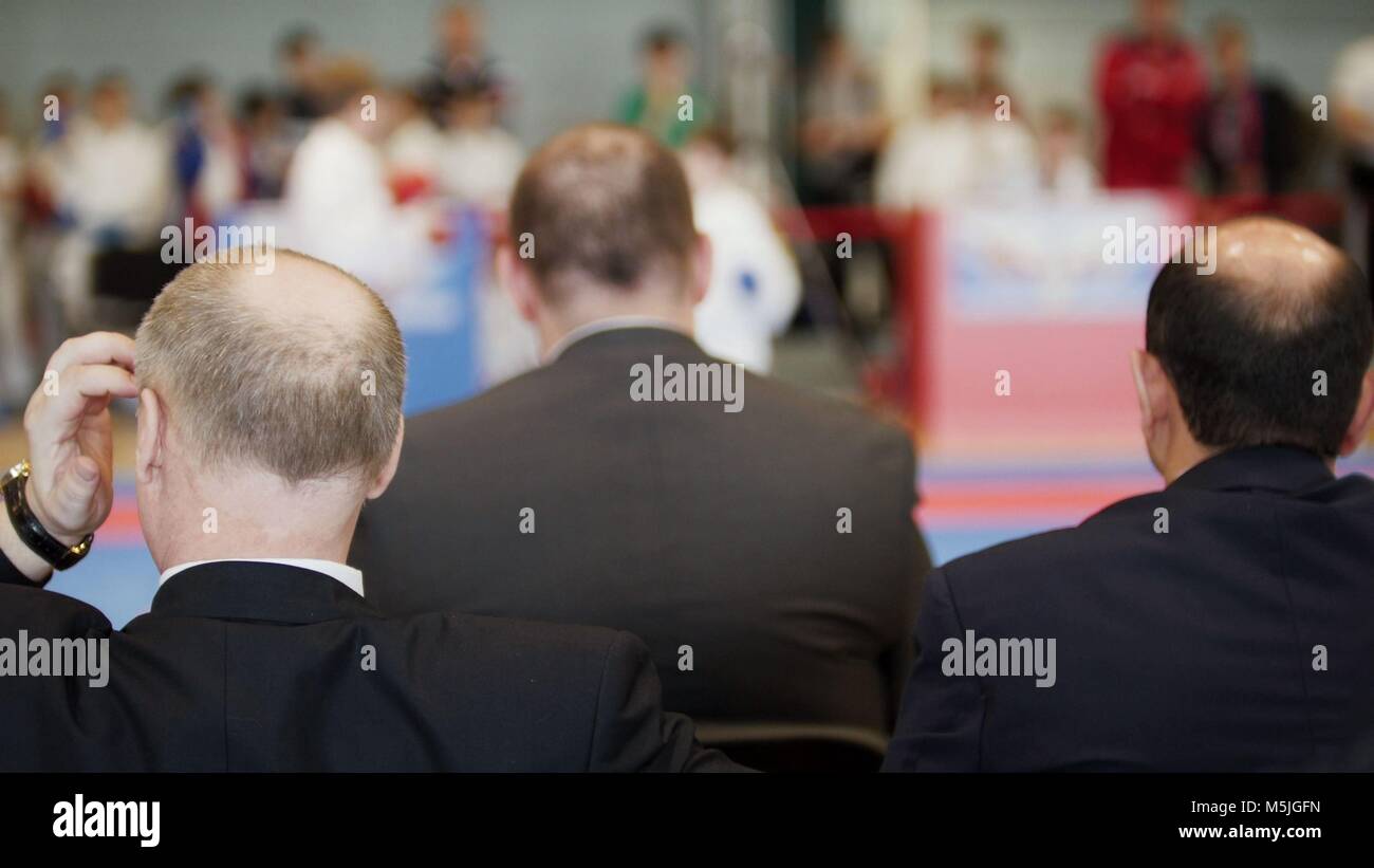 Martial art competitions - three bald men coaches looking at karate kid ...