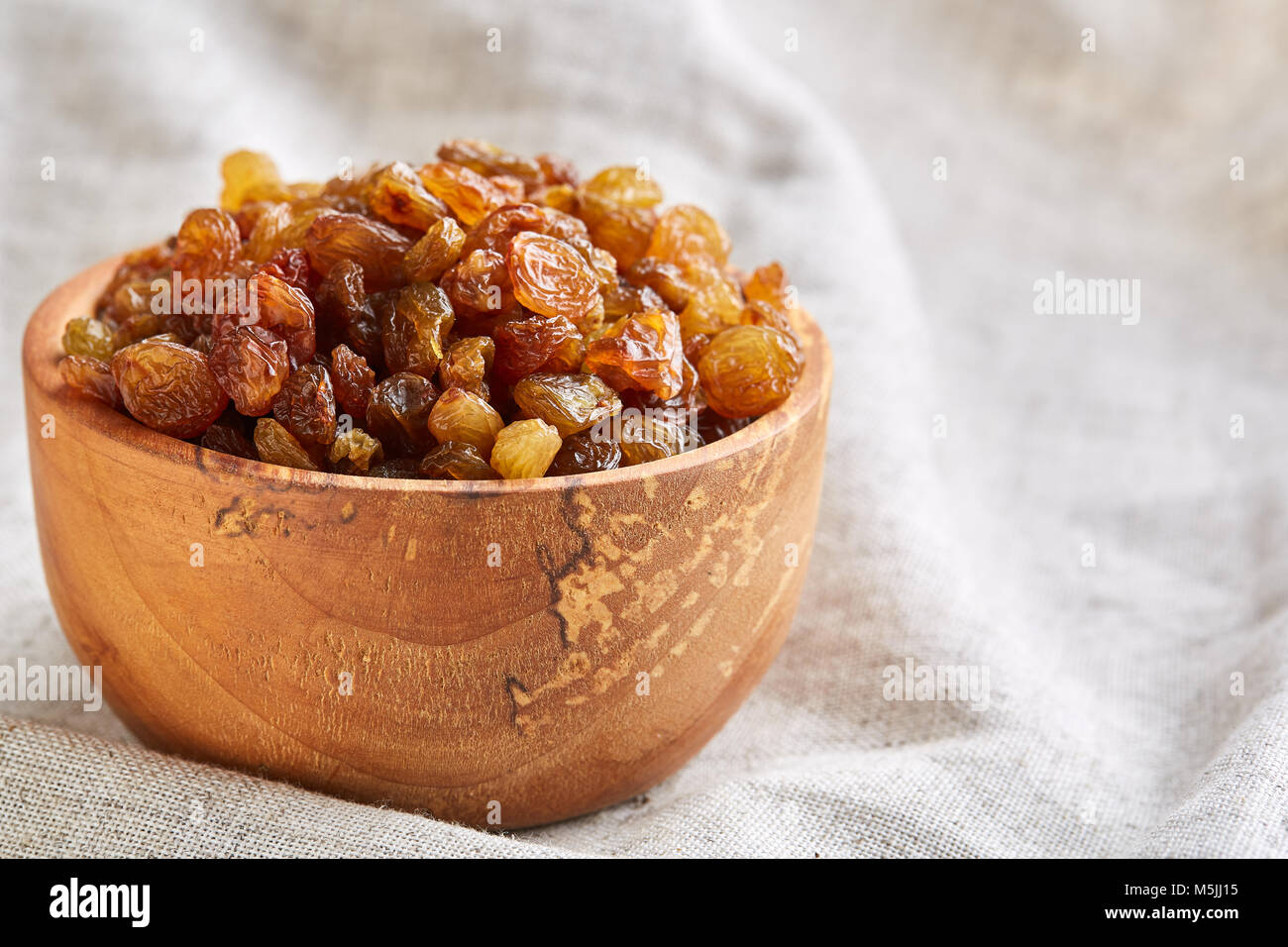 Close-up picture of wooden bowl with golden raisins on light grey ...