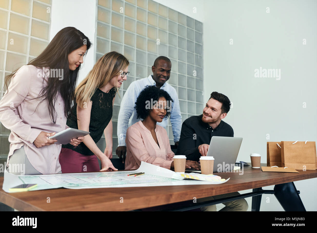 Diverse group of smiling designers using a laptop and discussing ...