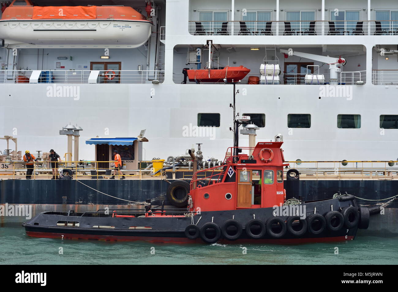 Tug with barge at large white cruise ship side Stock Photo - Alamy