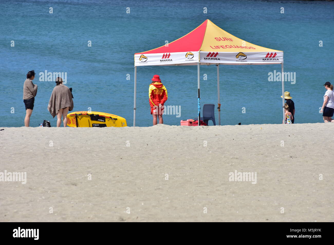 Surf lifeguard using gazebo as shelter on sandy beach on bright sunny ...