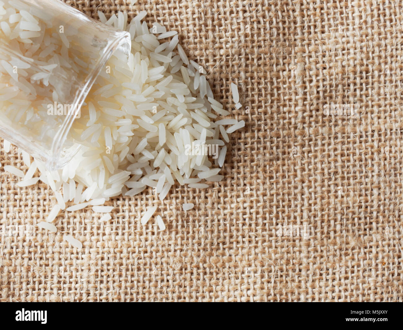 White raw rice drop from footed shot glass over brown sackcloth ...