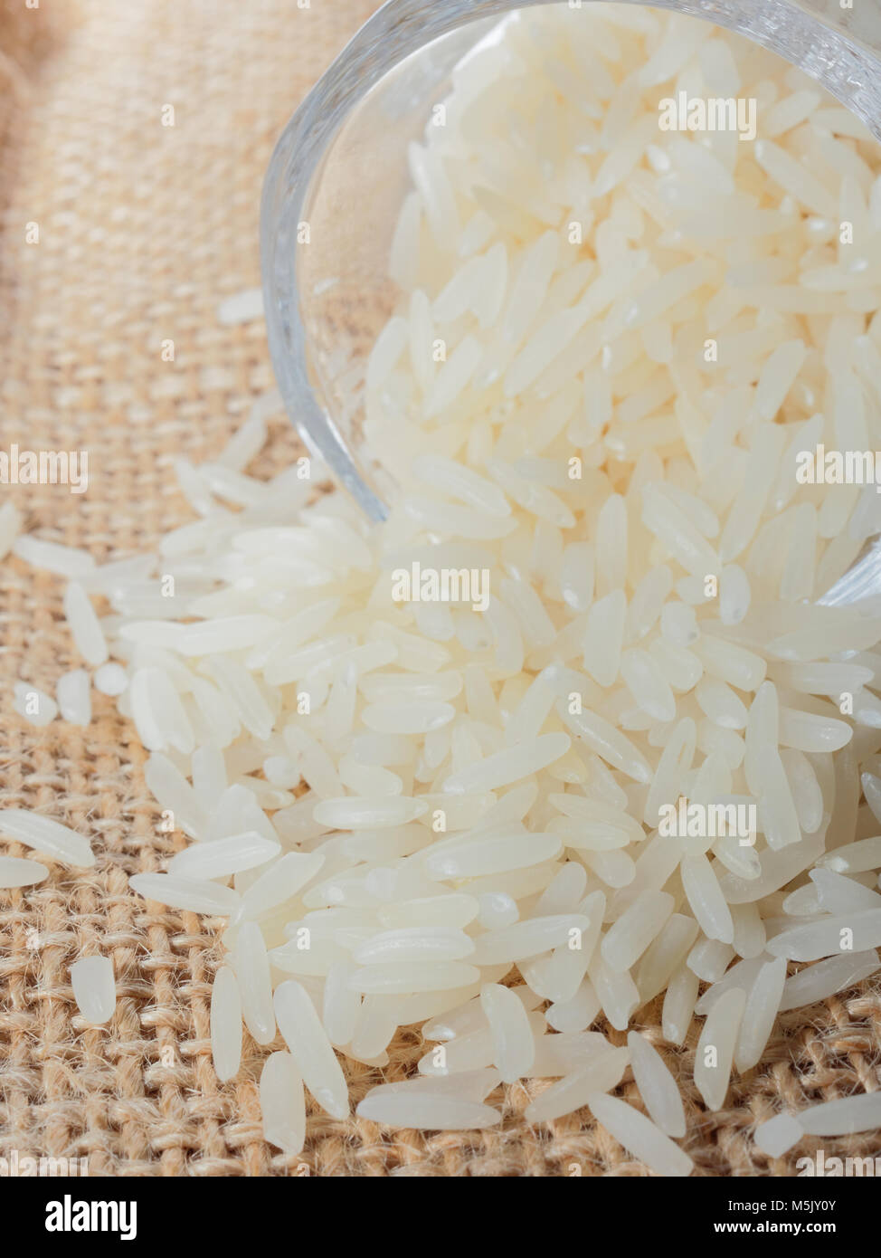 White raw rice drop from footed shot glass over brown sackcloth ...