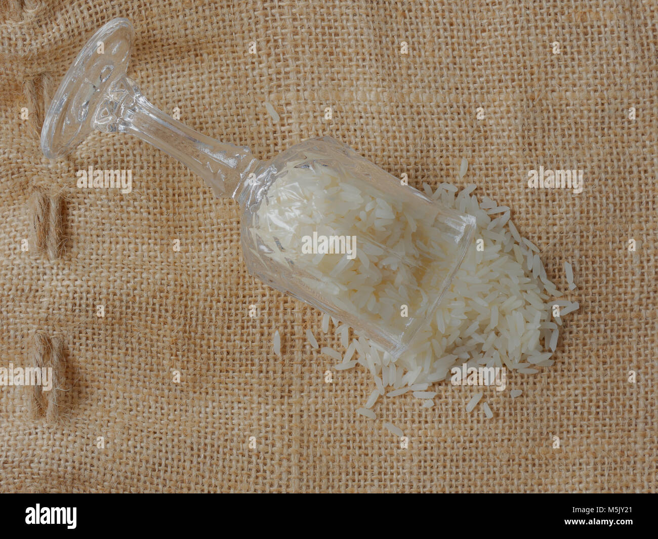 White raw rice drop from footed shot glass over brown sackcloth ...