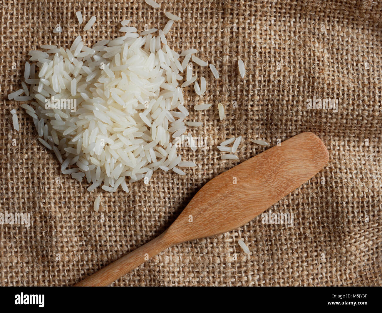 White raw rice with wooden spatula over brown sackcloth background ...