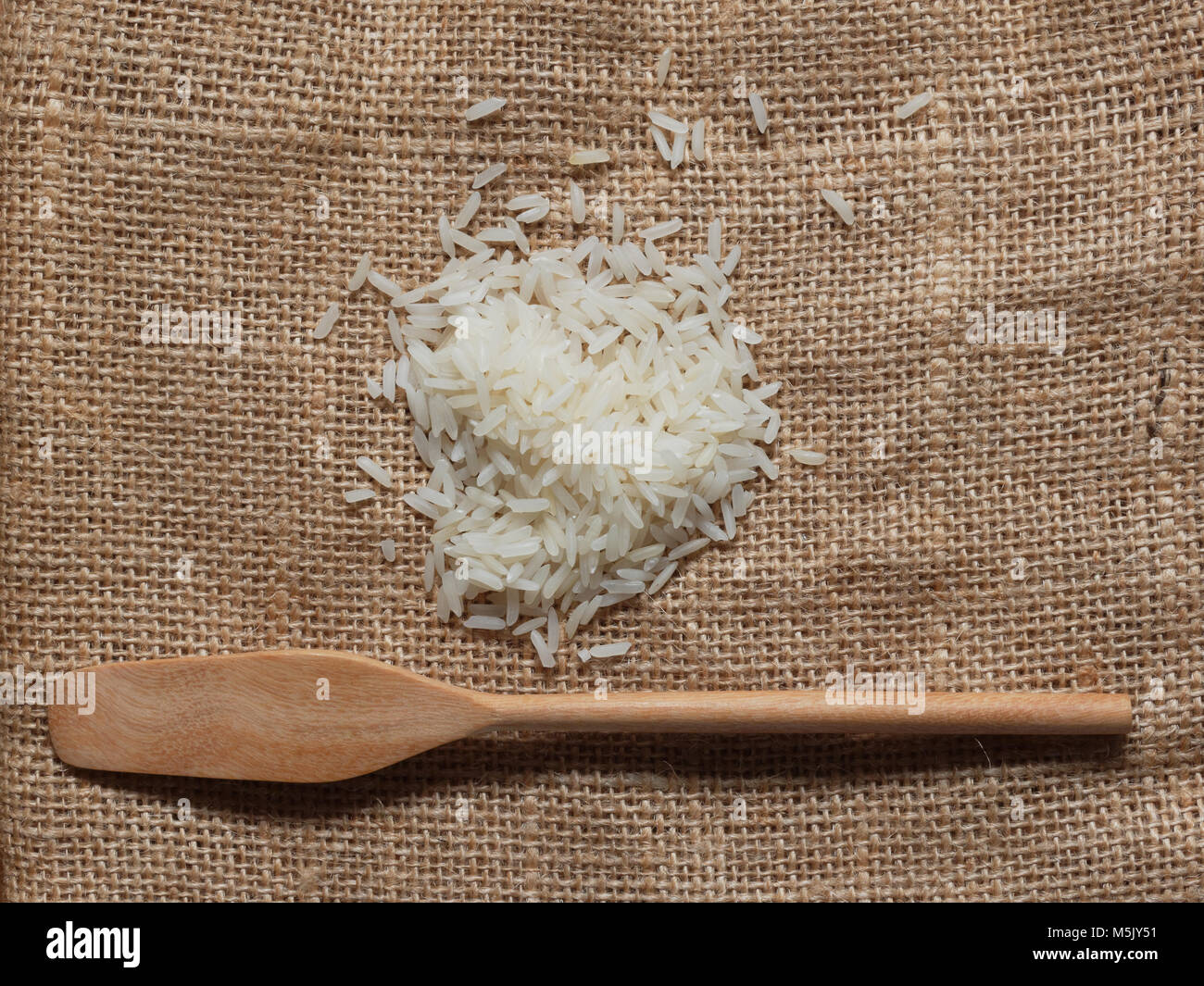 White raw rice with wooden spatula over brown sackcloth background ...