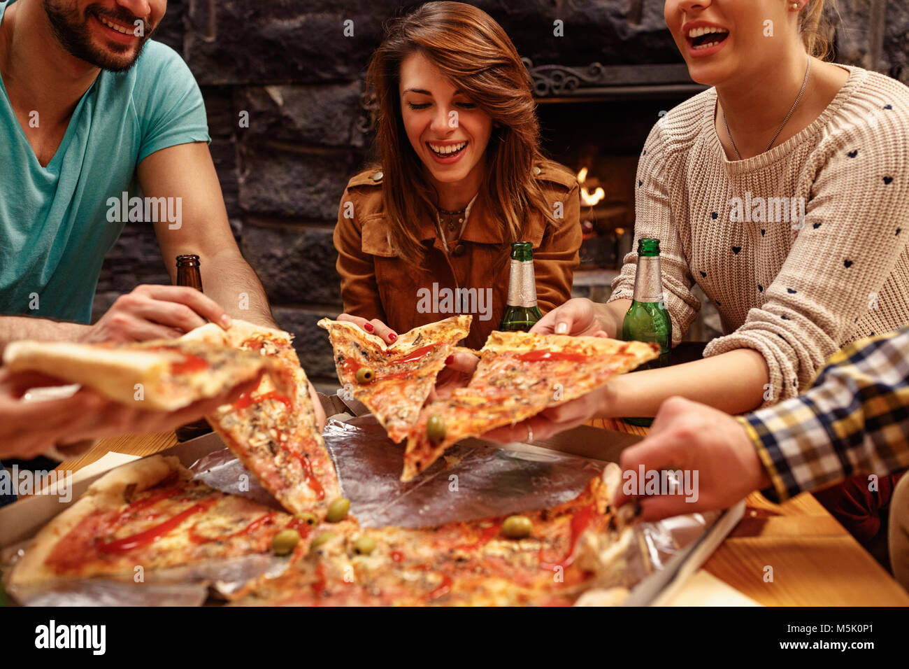 Young laughing friends eating pizza and having fun. They are enjoying ...