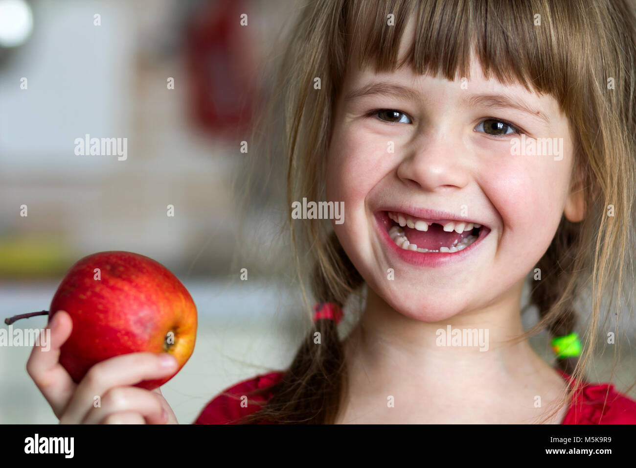 A cute little curly toothless girl smiles and holds a red apple ...