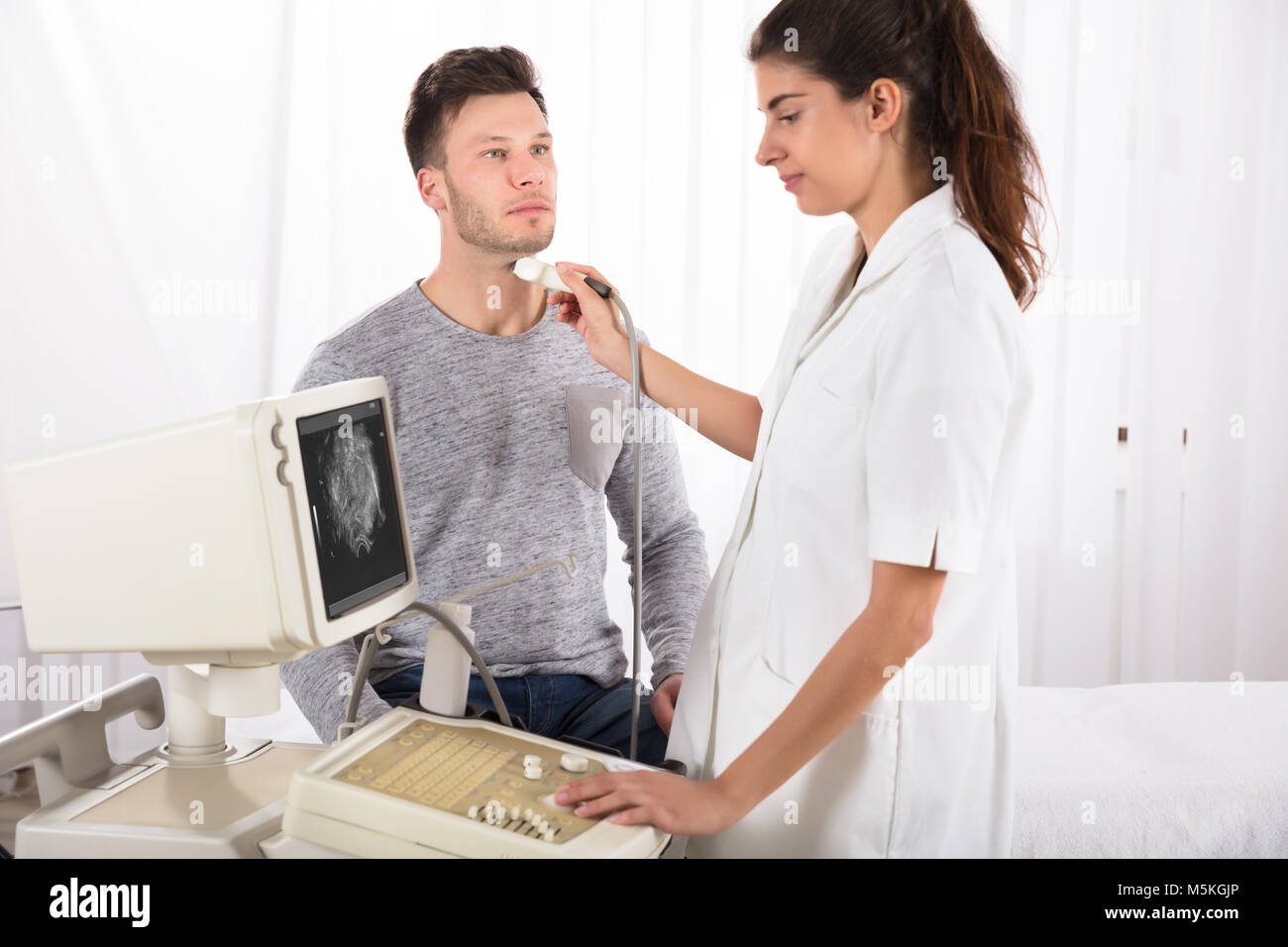 Young Man Getting Ultrasound Scan On Neck By Young Female Doctor In ...