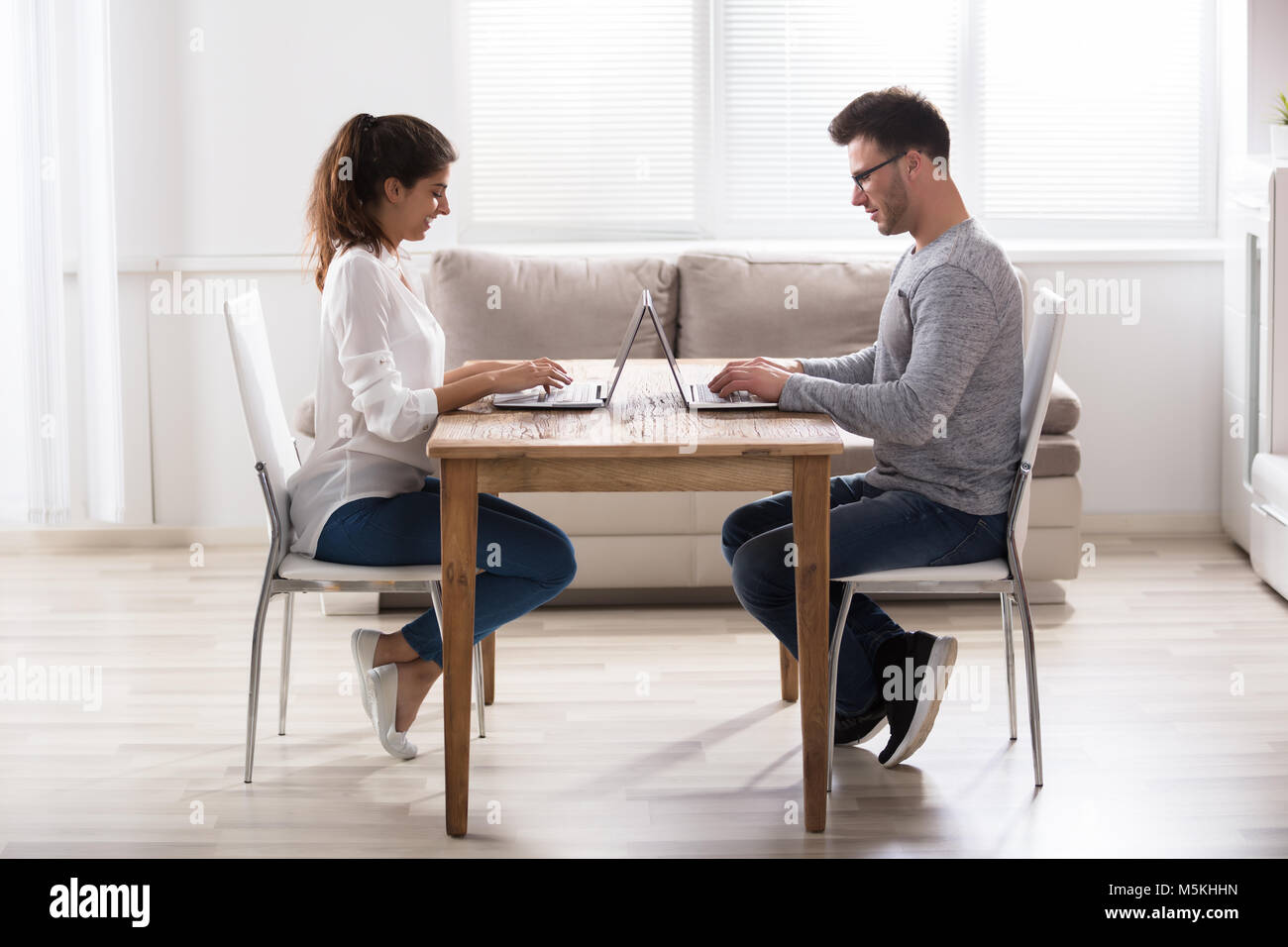 Happy Young Couple Sitting Face To Face Using Laptop Over The Table At ...