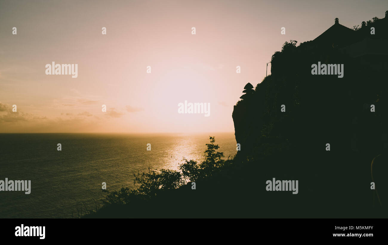 The sunset is seen across the sea from a temple on the cliffs in ...