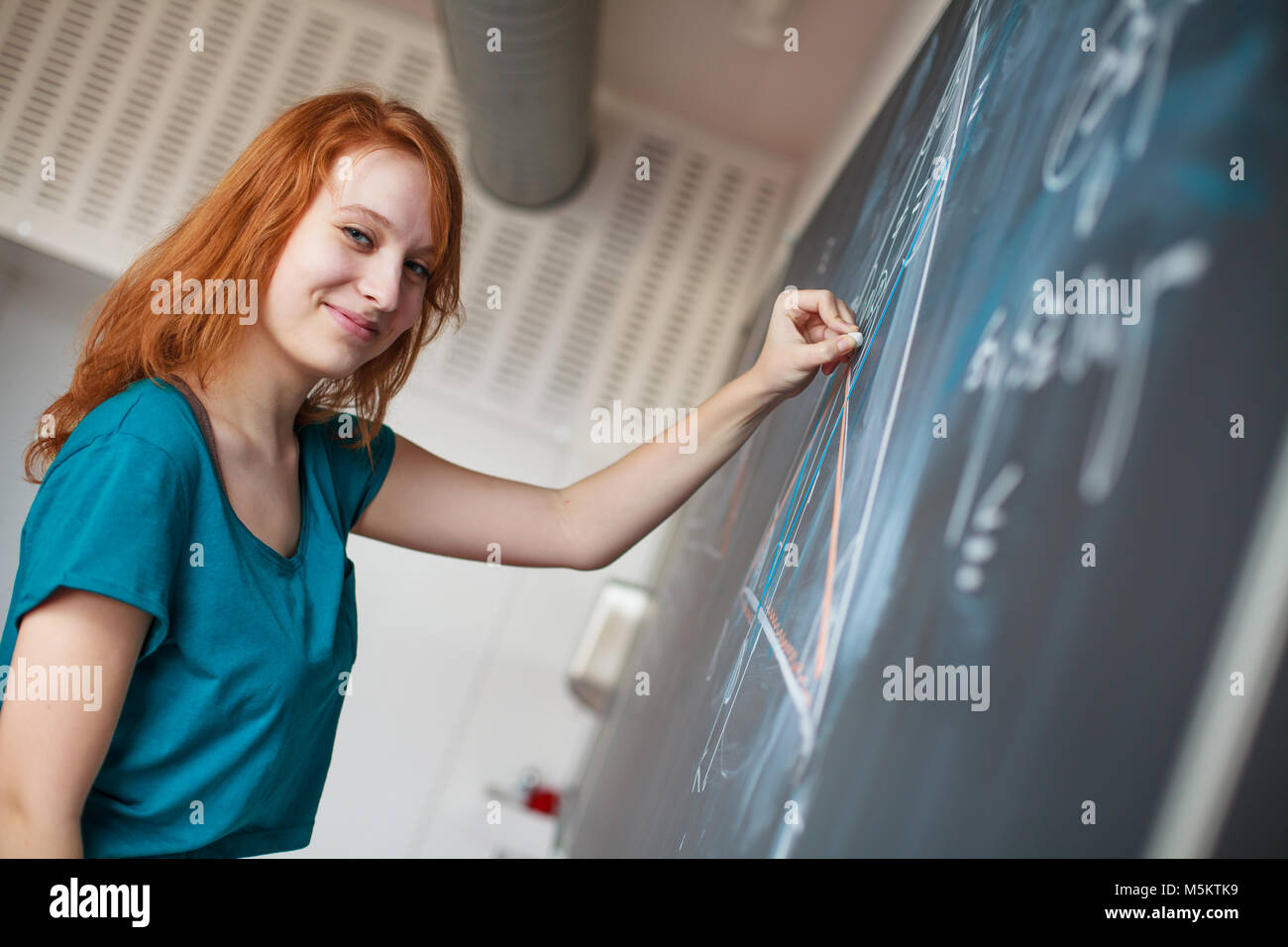 Portrait of a pretty young college student writing on the blackboard ...