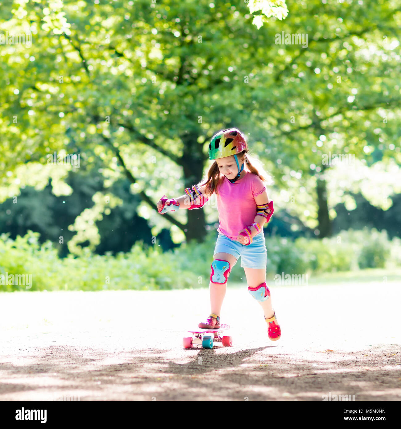Child riding skateboard in summer park. Little girl learning to ride ...