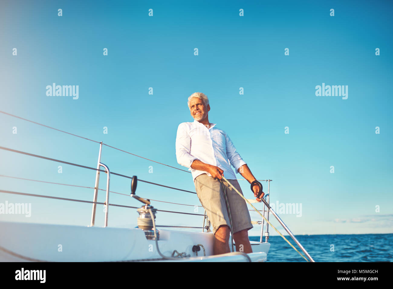 Smiling mature man standing alone on the deck of his boat steering with ...