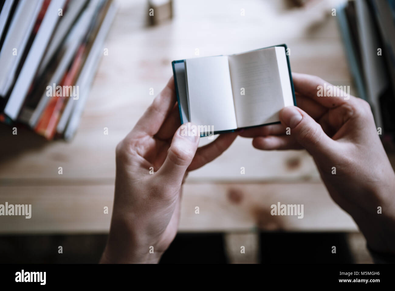 A man reading a miniature book among the big books in the library Stock ...