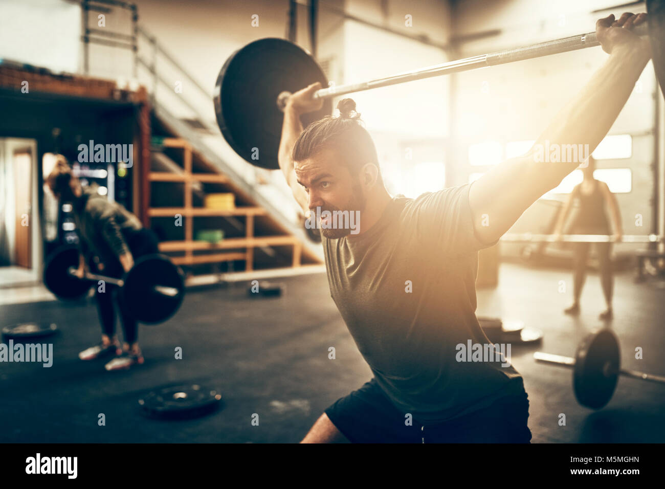 Fit and focused young man straining to lift heavy weights over his head ...