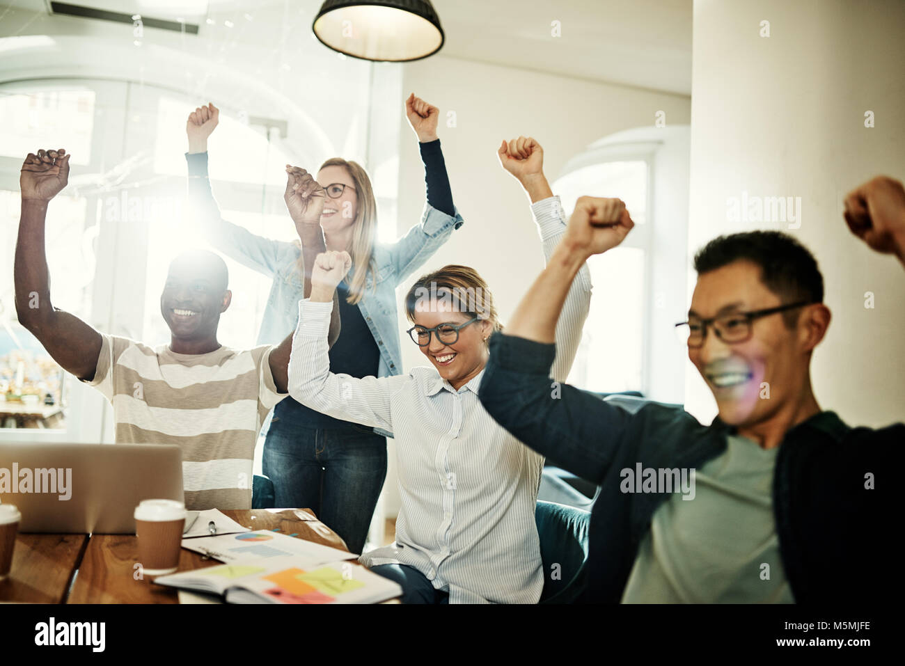 Excited group of diverse businesspeople cheering during a meeting while ...