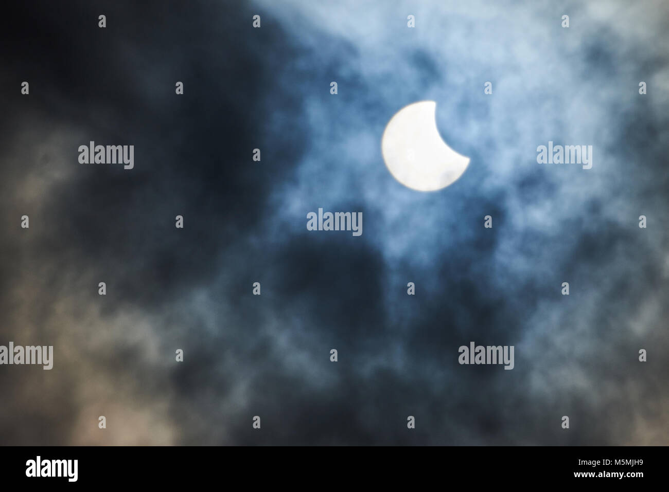 Real solar partial eclipse on blue cloudy sky background Stock Photo ...