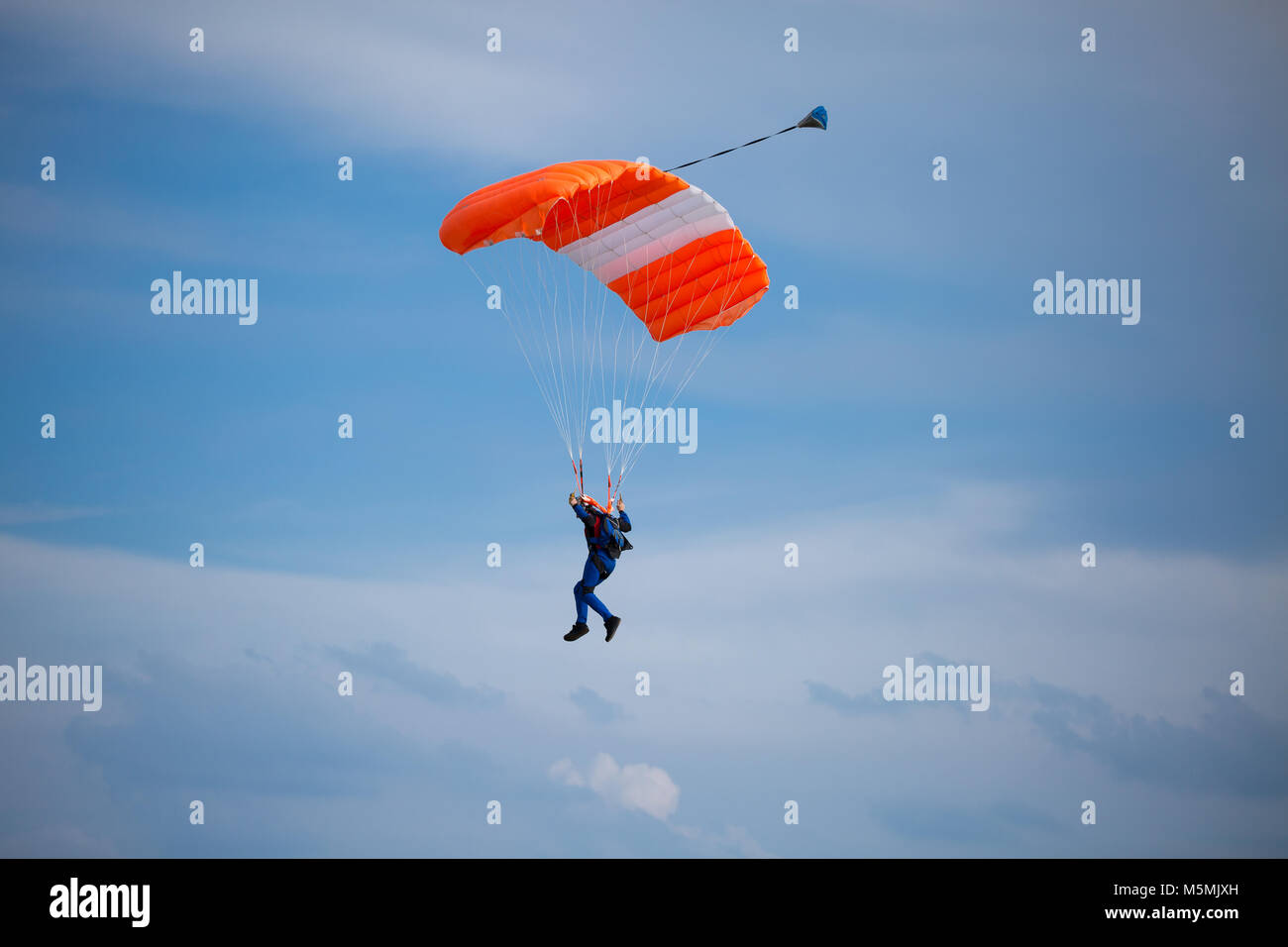 Parachutist with Orange Parachute against Blue Sky preparing for ...