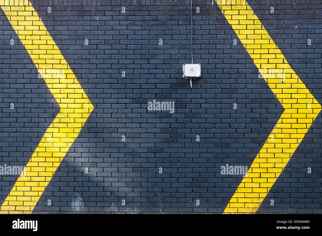 Two large yellow chevrons indicating direction painted on a brick wall ...