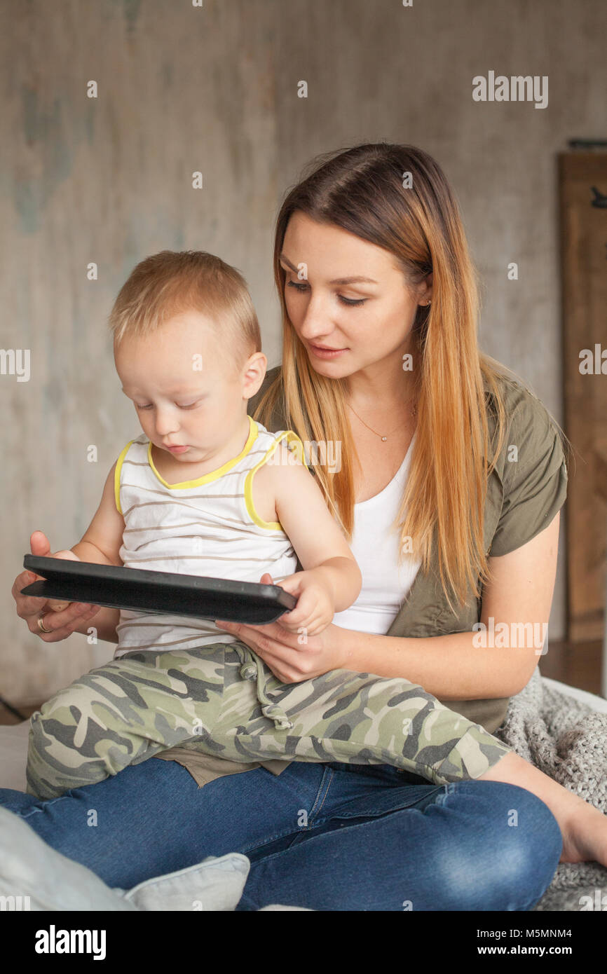 Mother and son sitting on sofa using digital tablet. Mom and little boy ...