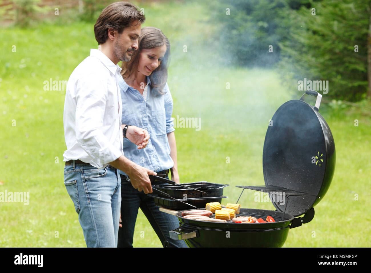 Happy couple cooking food on barbecue Stock Photo - Alamy