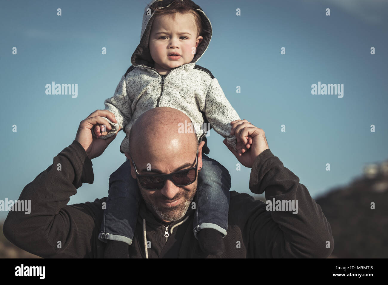 Child is sitting on his father's shoulders, handsome dad playing with ...