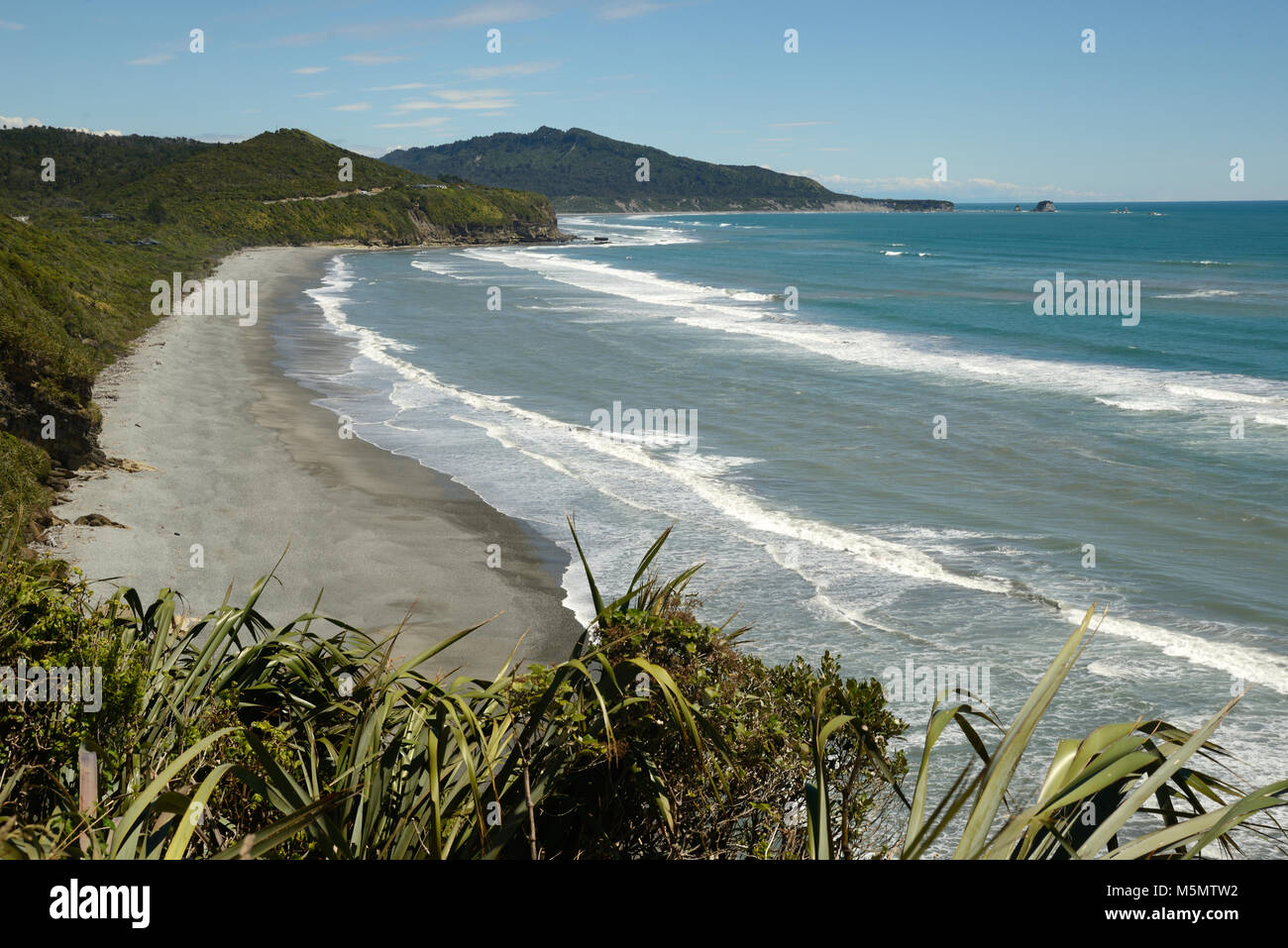 native bush frames a beach at low tide on a West Coast beach, South ...