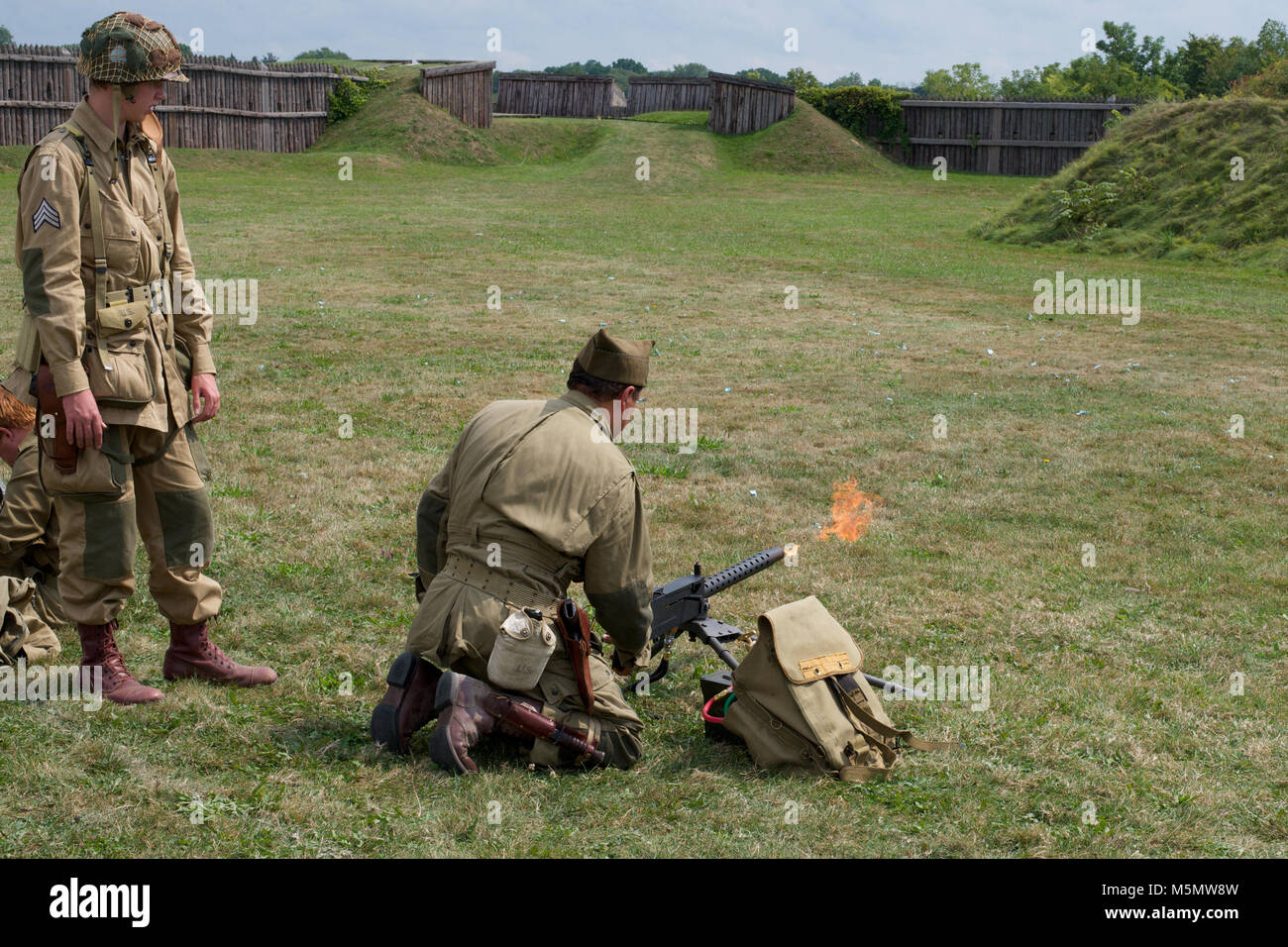 A soldier dressed in WWII uniform firing a machine gun at a reenactment ...