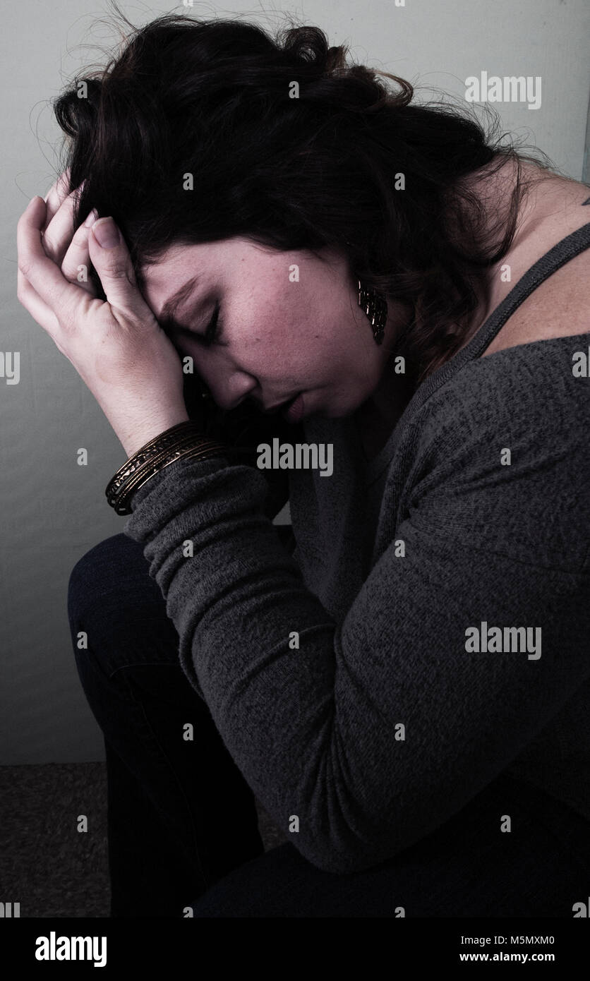 Young woman sitting with her hand to her face looking upset Stock Photo ...