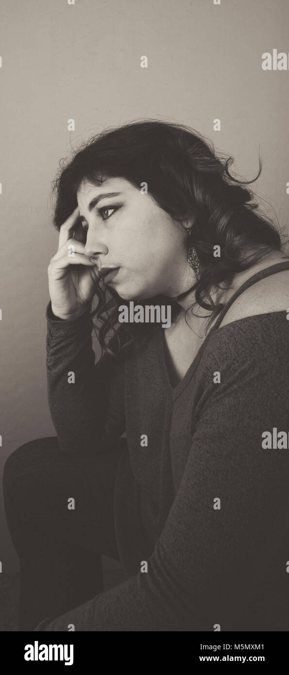 Young woman sitting with her hand to her face looking upset Stock Photo ...