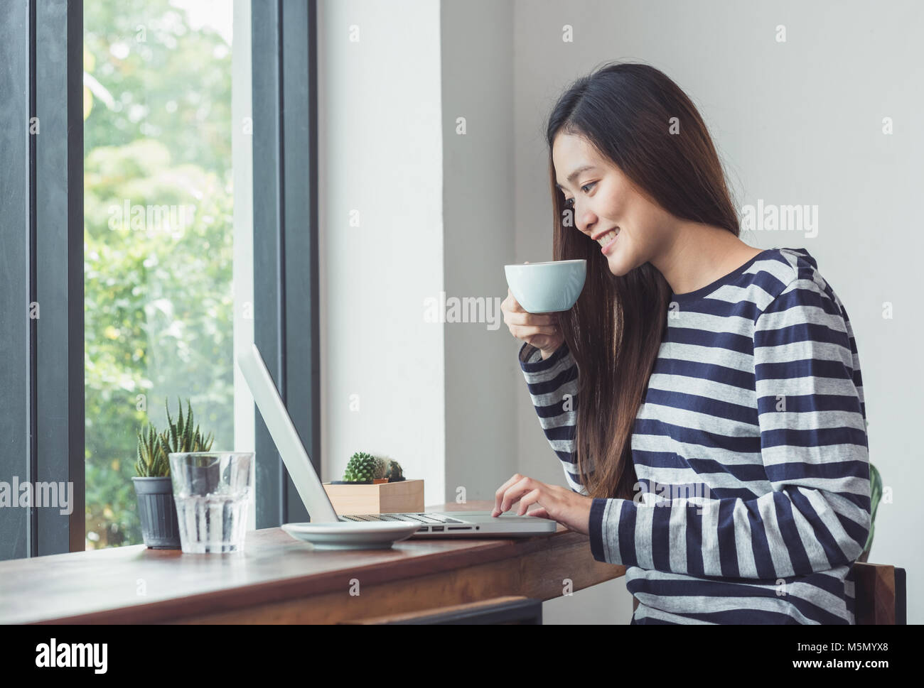 Asian woman using on laptop computer near window at cafe restaurant ...