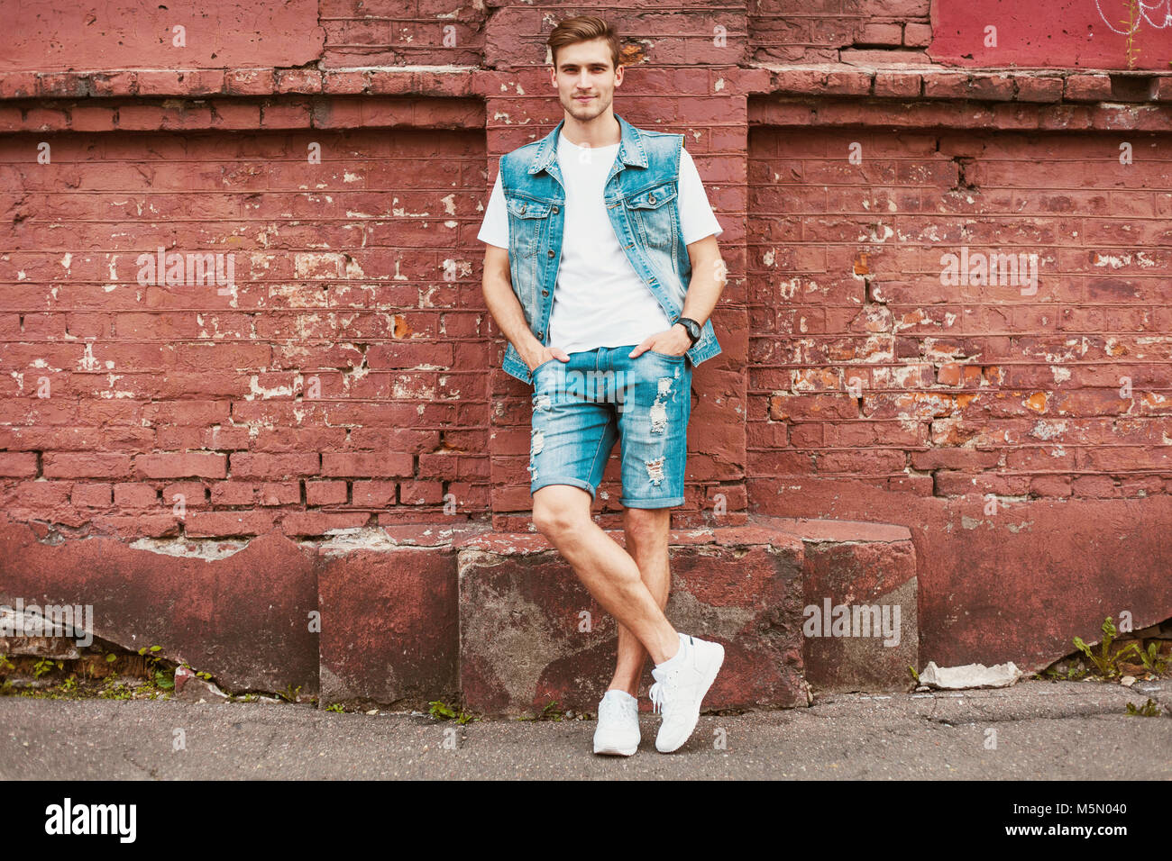 casual young man stands with his back against a brick wall Stock Photo ...