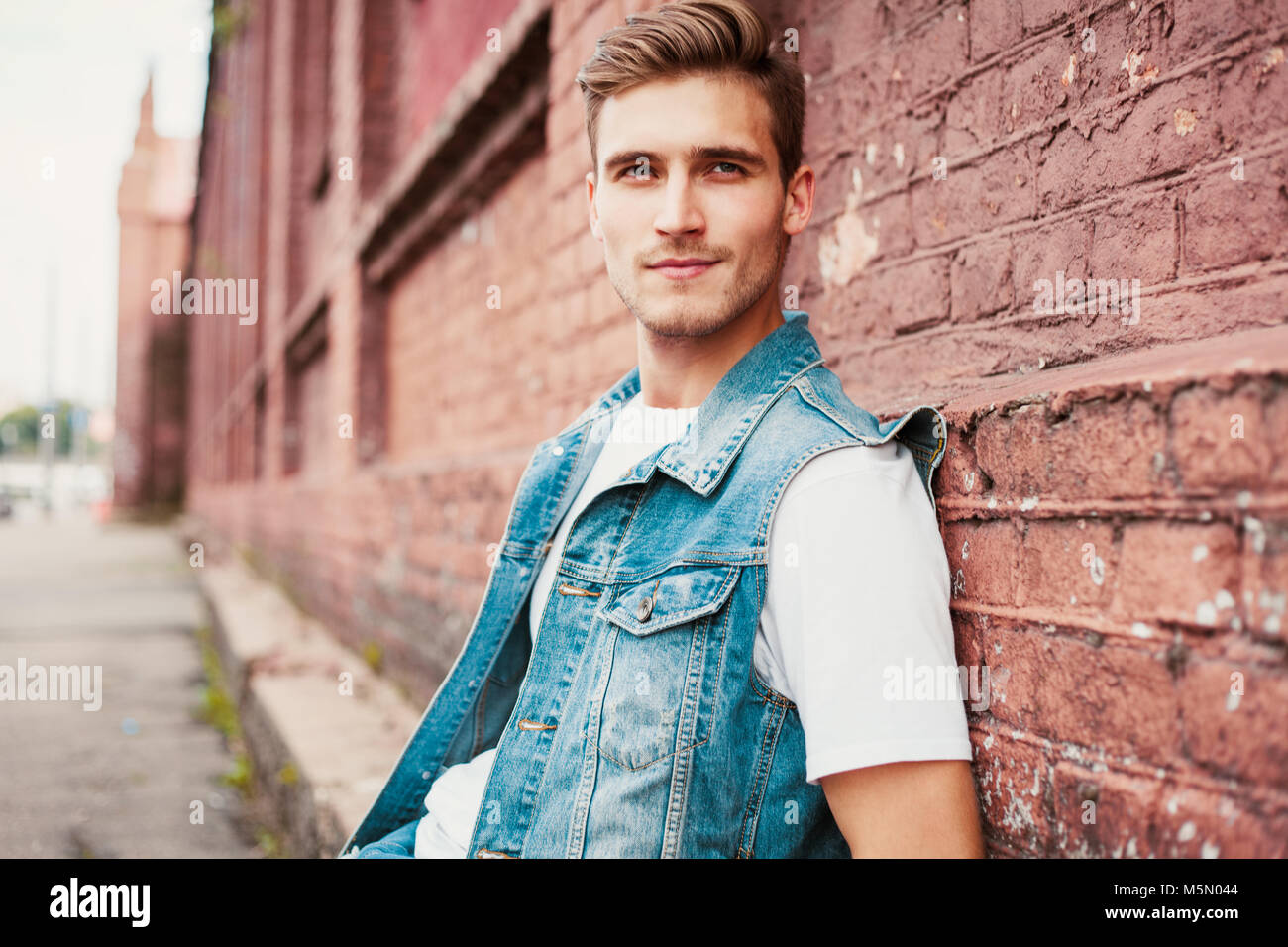 casual young man stands with his back against a brick wall Stock Photo ...