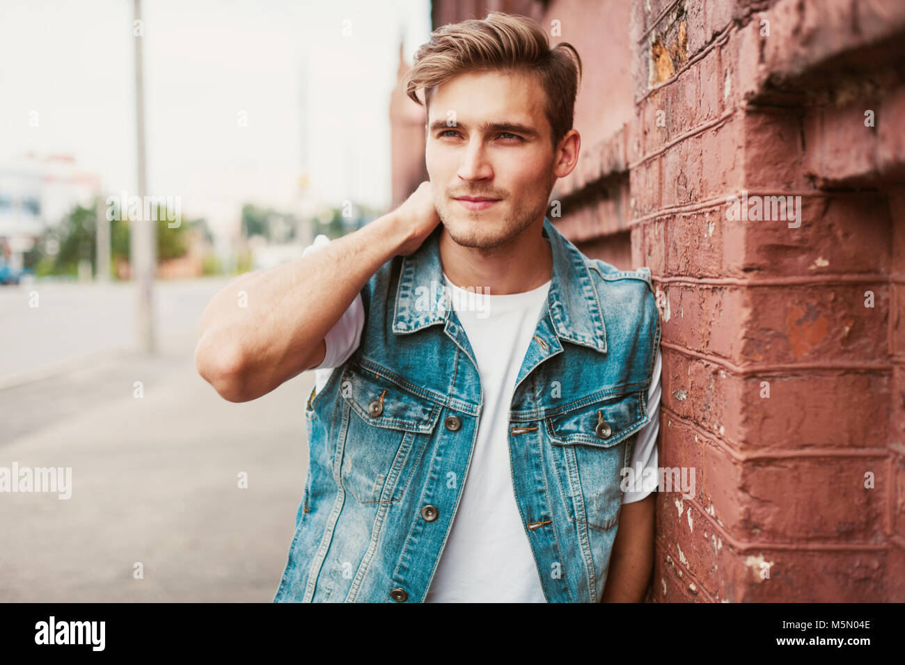 casual young man stands with his back against a brick wall Stock Photo ...