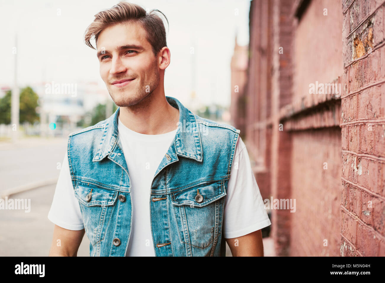 casual young man stands with his back against a brick wall Stock Photo ...