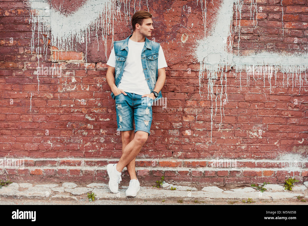 casual young man stands with his back against a brick wall Stock Photo ...