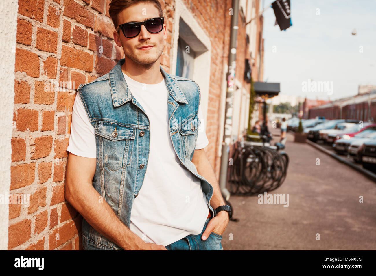casual young man stands with his back against a brick wall Stock Photo ...