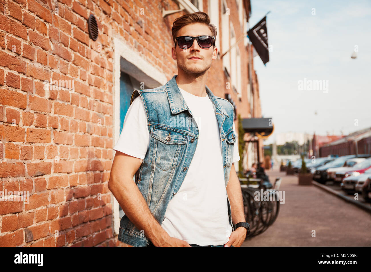 casual young man stands with his back against a brick wall Stock Photo ...